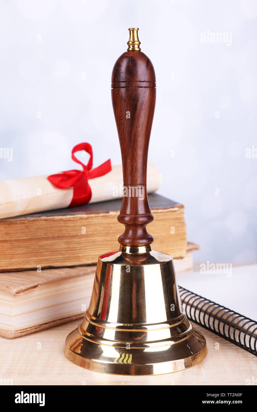Gold school bell with school supplies on table on bright background ...