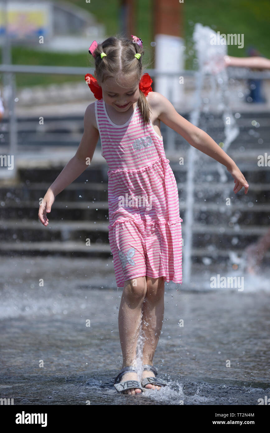 Strong heat in the city: little girl playing with fountain water jets ...