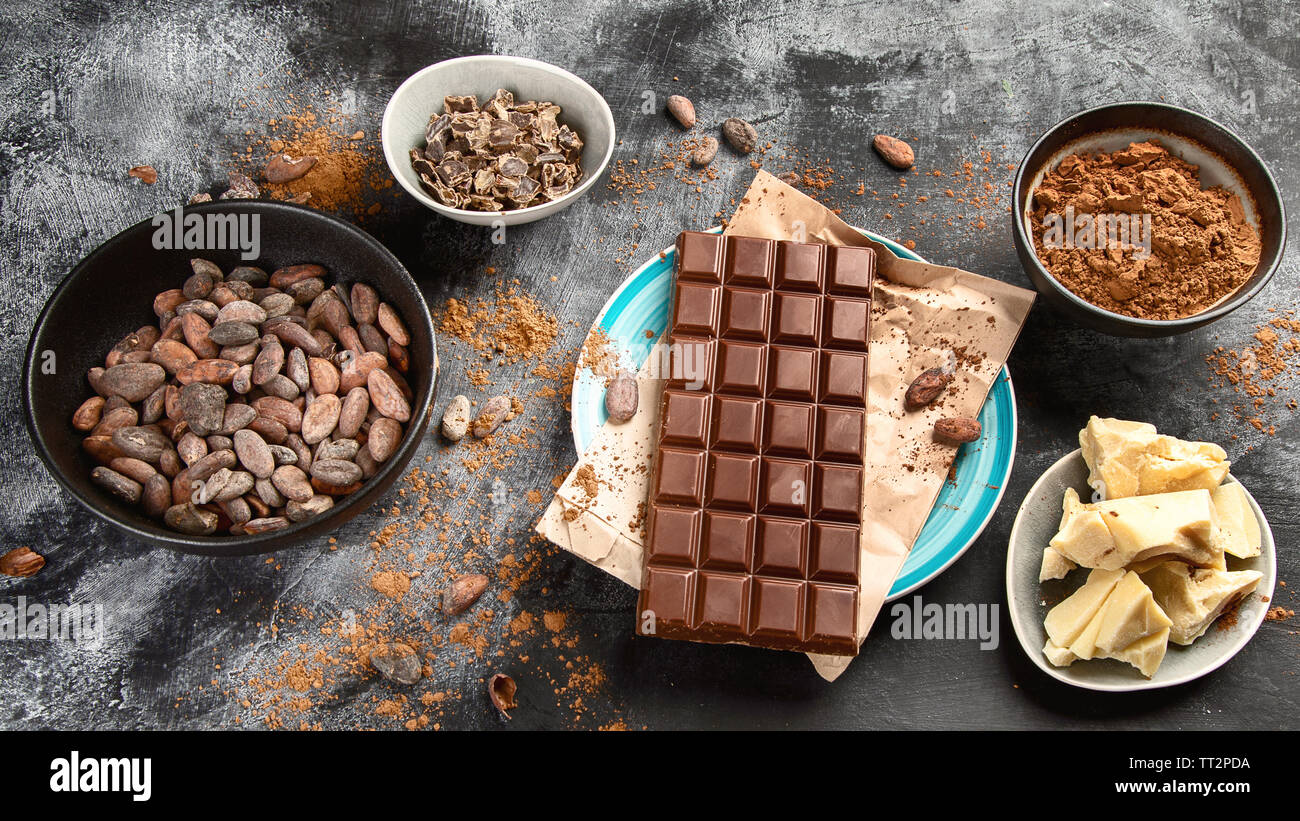 Cacao beans, powder, cacao butter and chocolate bar on dark background ...