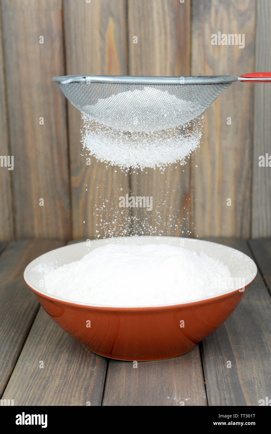 Sifting flour into bowl on table on wooden background Stock Photo - Alamy