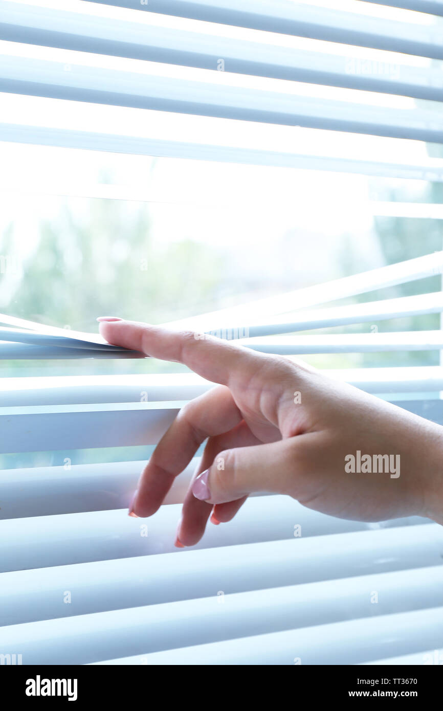 Female hand separating slats of venetian blinds with a finger to see ...