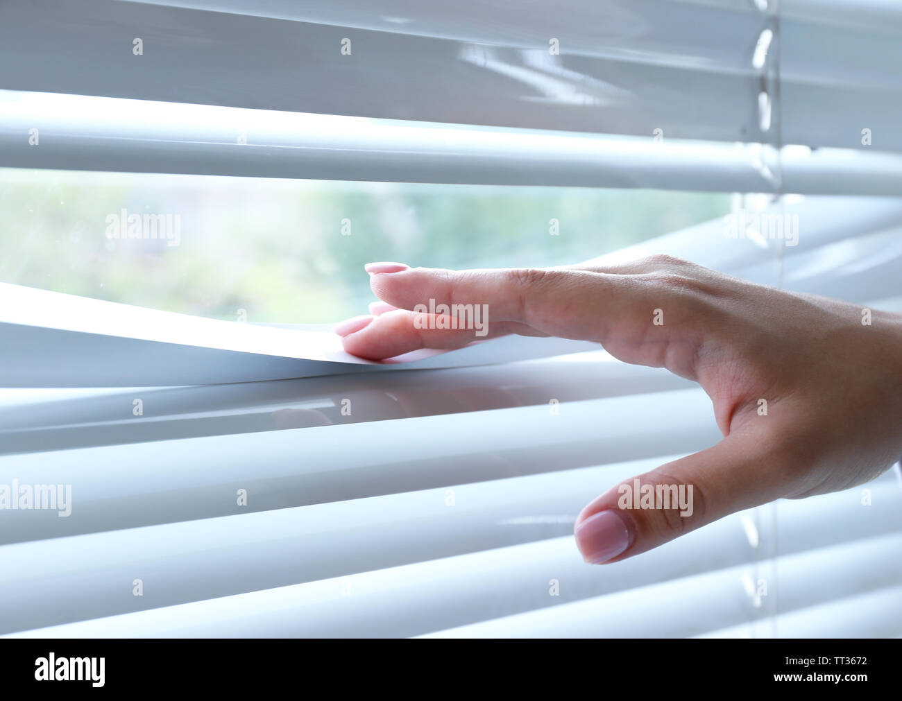 Female hand separating slats of venetian blinds with a finger to see ...
