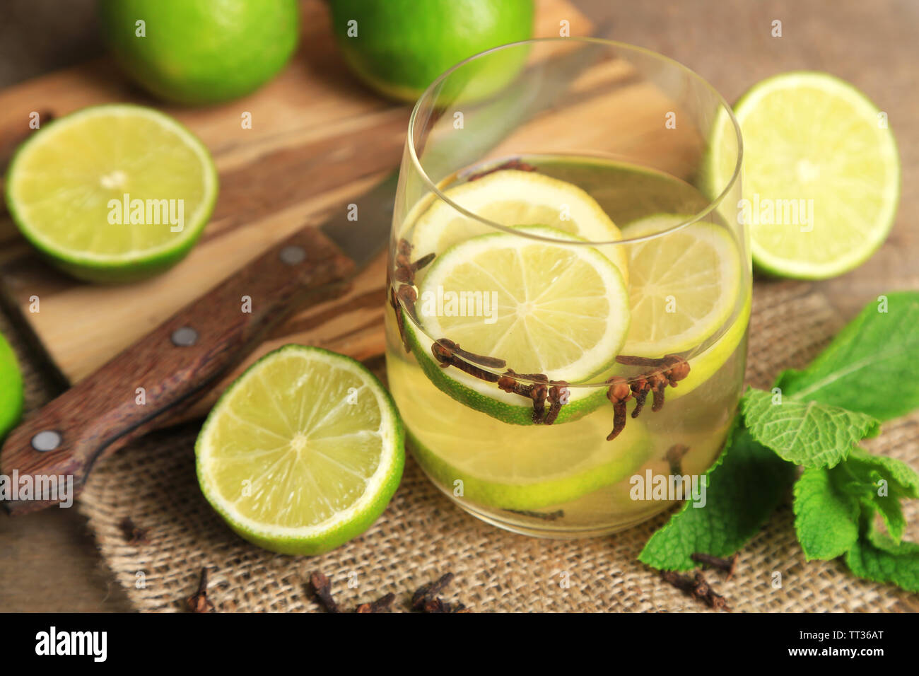 Fresh summer drink with lime and cloves in glass, on color wooden ...