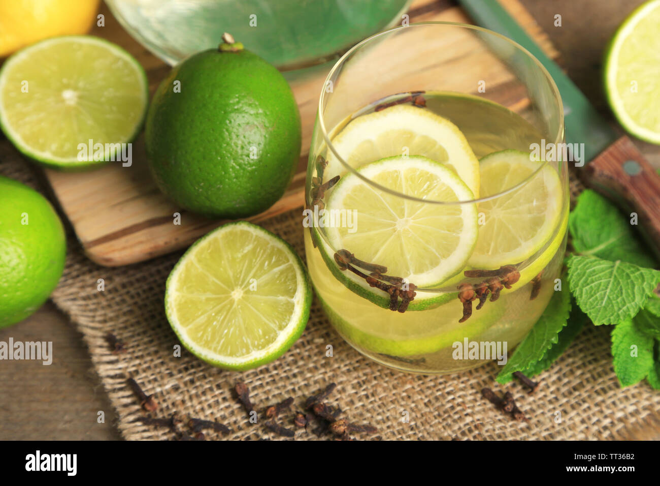 Fresh summer drink with lime and cloves in glass, on color wooden ...