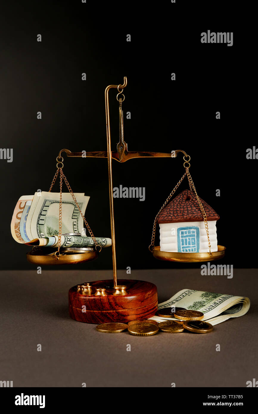 Scale with money and model of house on dark background Stock Photo - Alamy