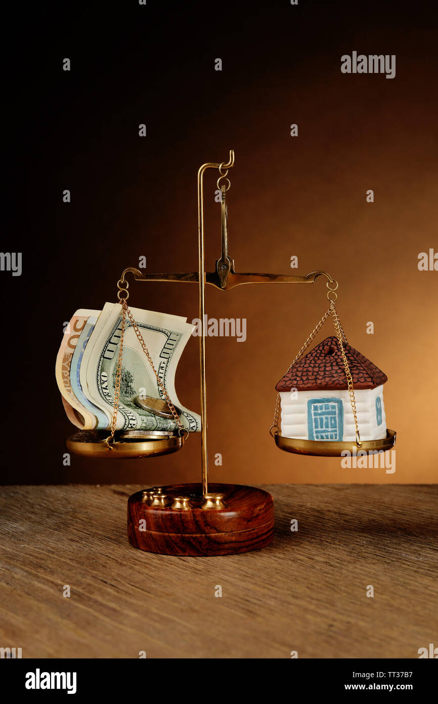 Scale with money and model of house on dark background Stock Photo - Alamy