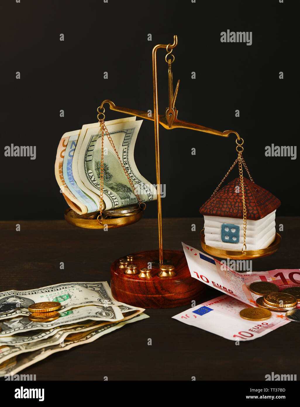 Scale with money and model of house on dark background Stock Photo - Alamy