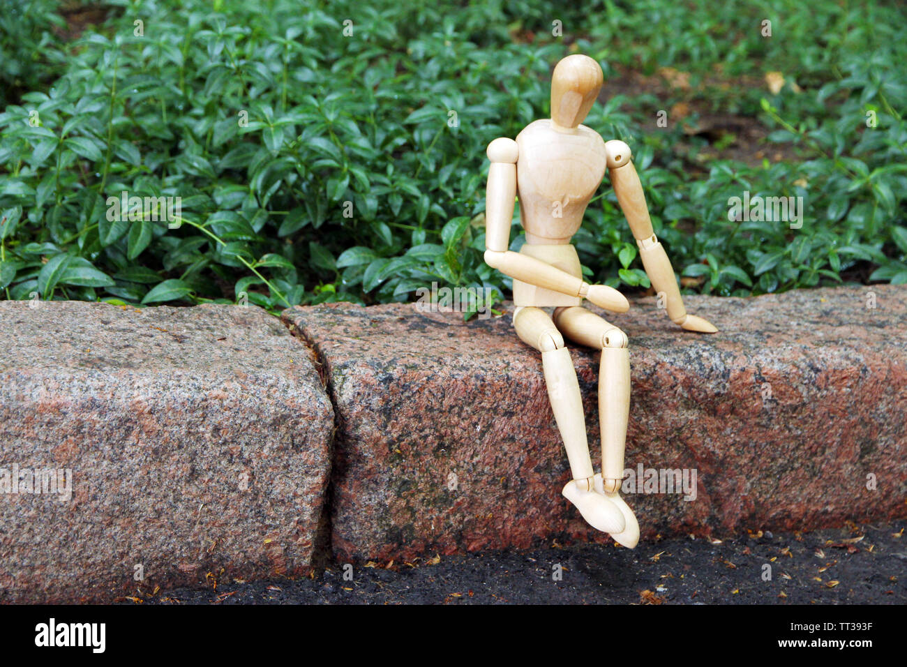 Wooden pose puppet sitting on stone, outdoors Stock Photo - Alamy
