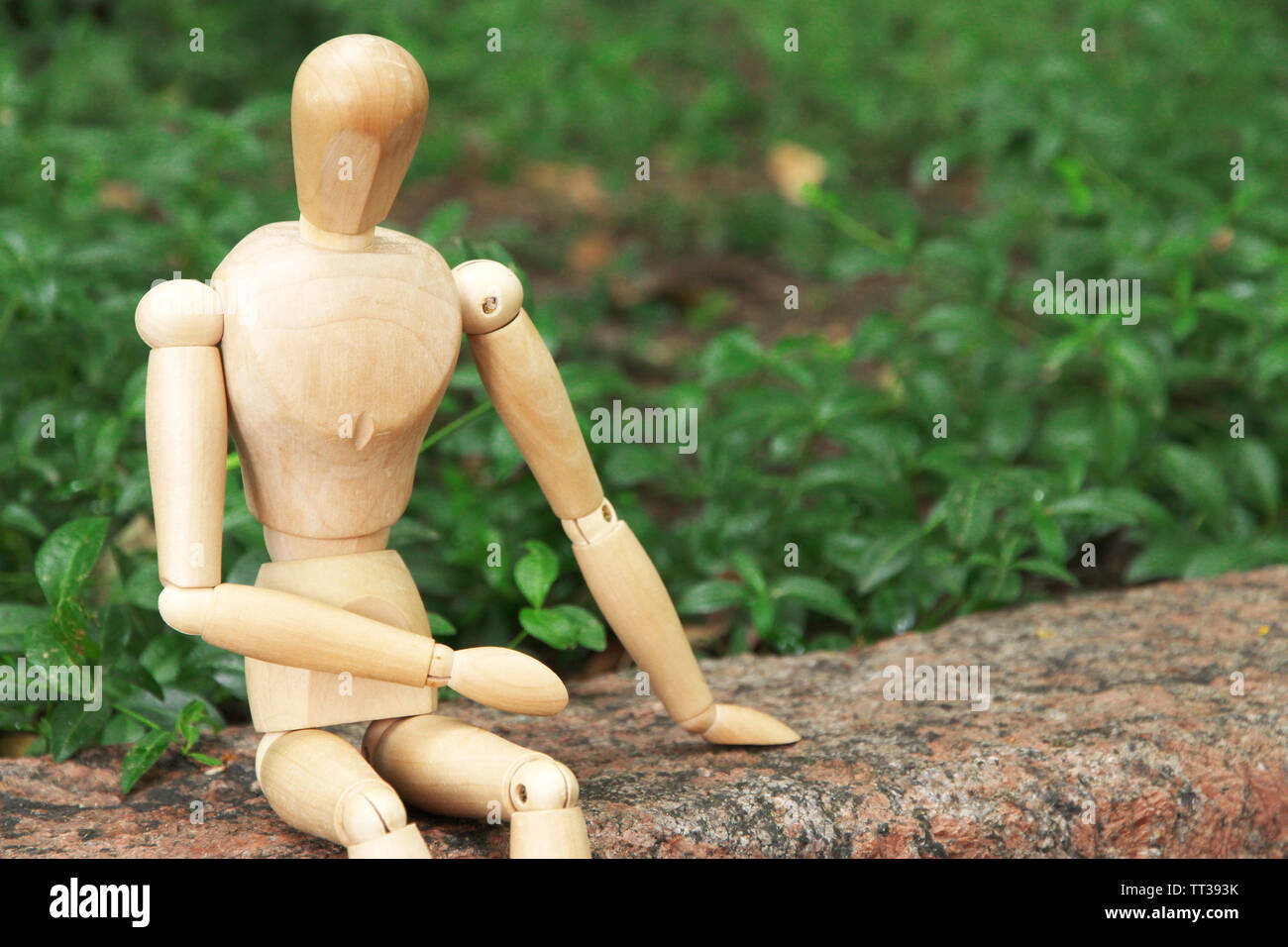 Wooden pose puppet sitting on stone, outdoors Stock Photo - Alamy