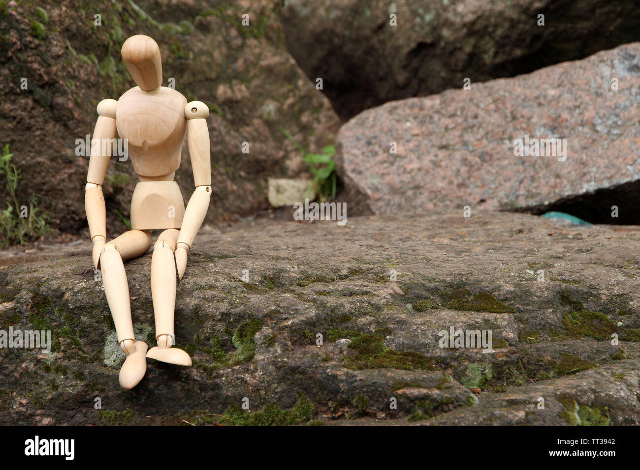 Wooden pose puppet sitting on stone, outdoors Stock Photo - Alamy