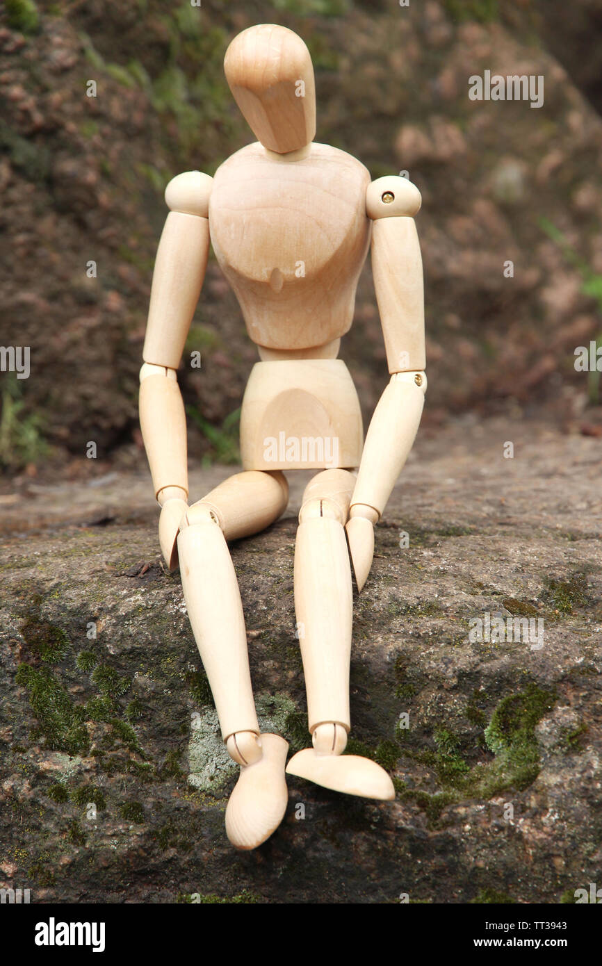Wooden pose puppet sitting on stone, outdoors Stock Photo - Alamy