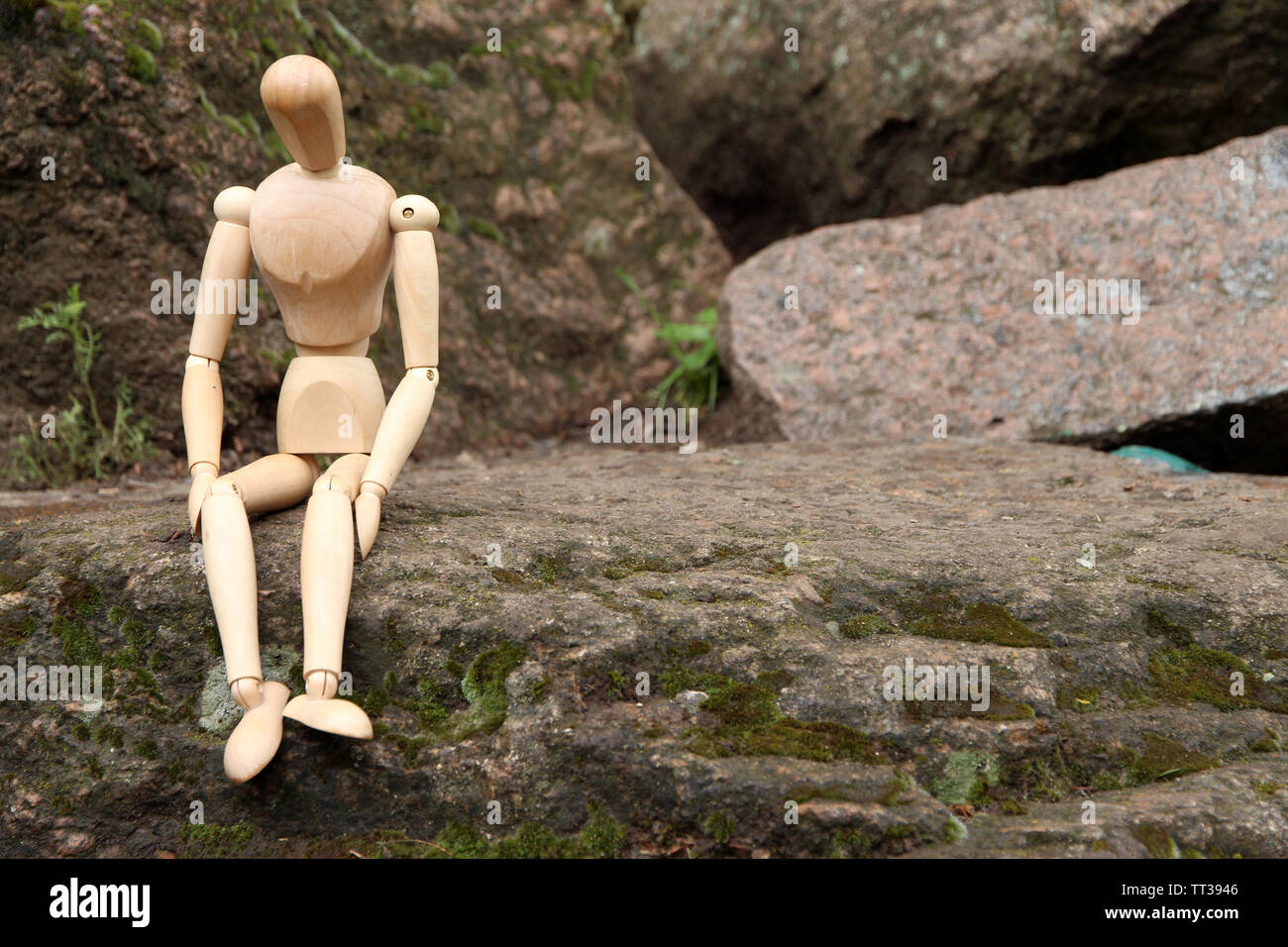 Wooden pose puppet sitting on stone, outdoors Stock Photo - Alamy