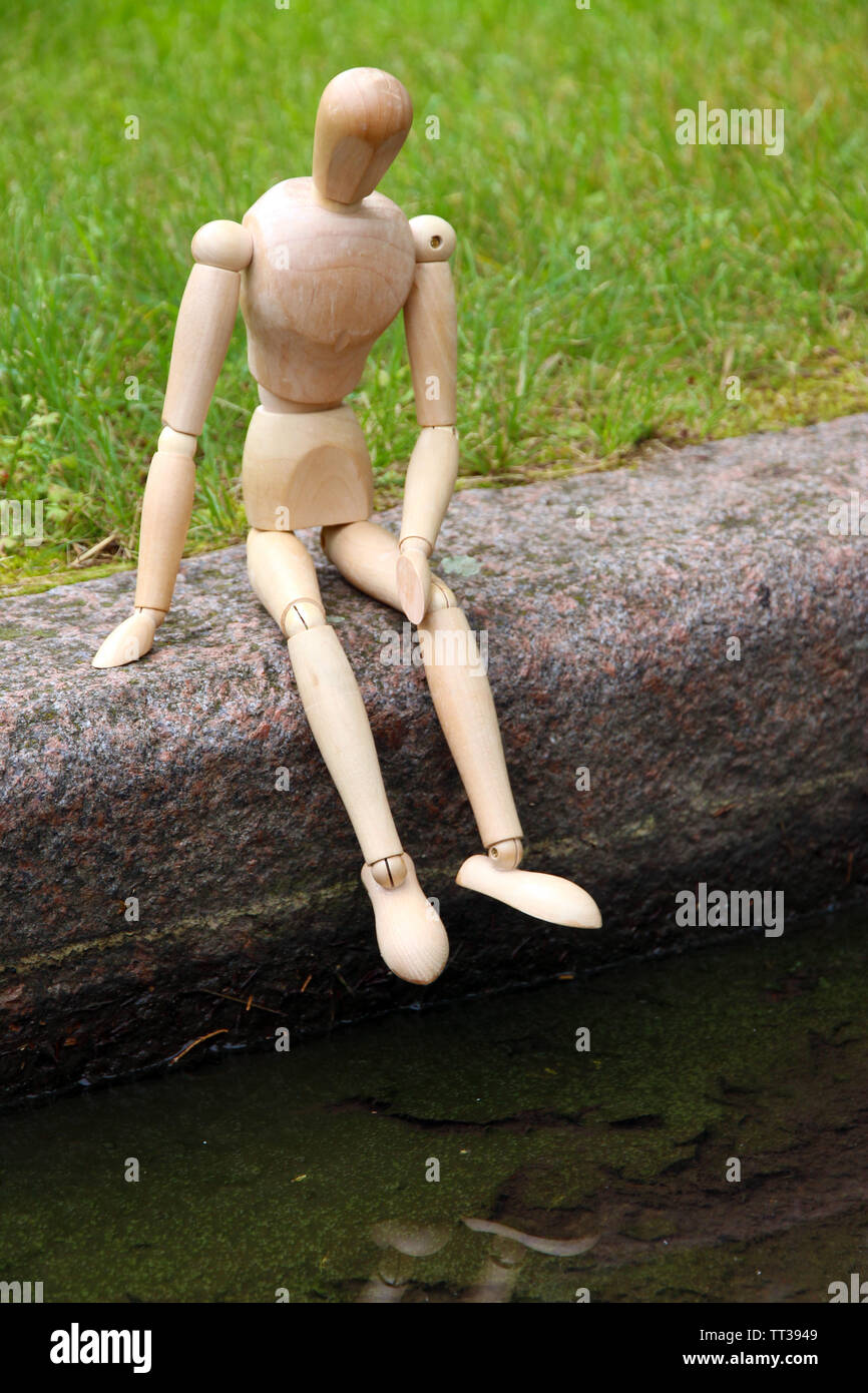 Wooden pose puppet sitting on stone, outdoors Stock Photo - Alamy