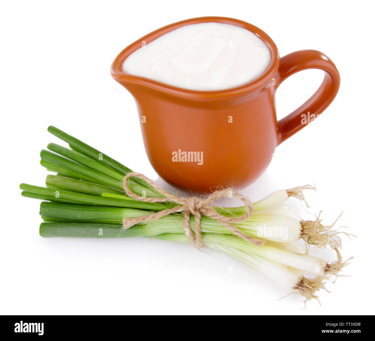 Clay pot with cream and a tuft of onion near it on white background ...