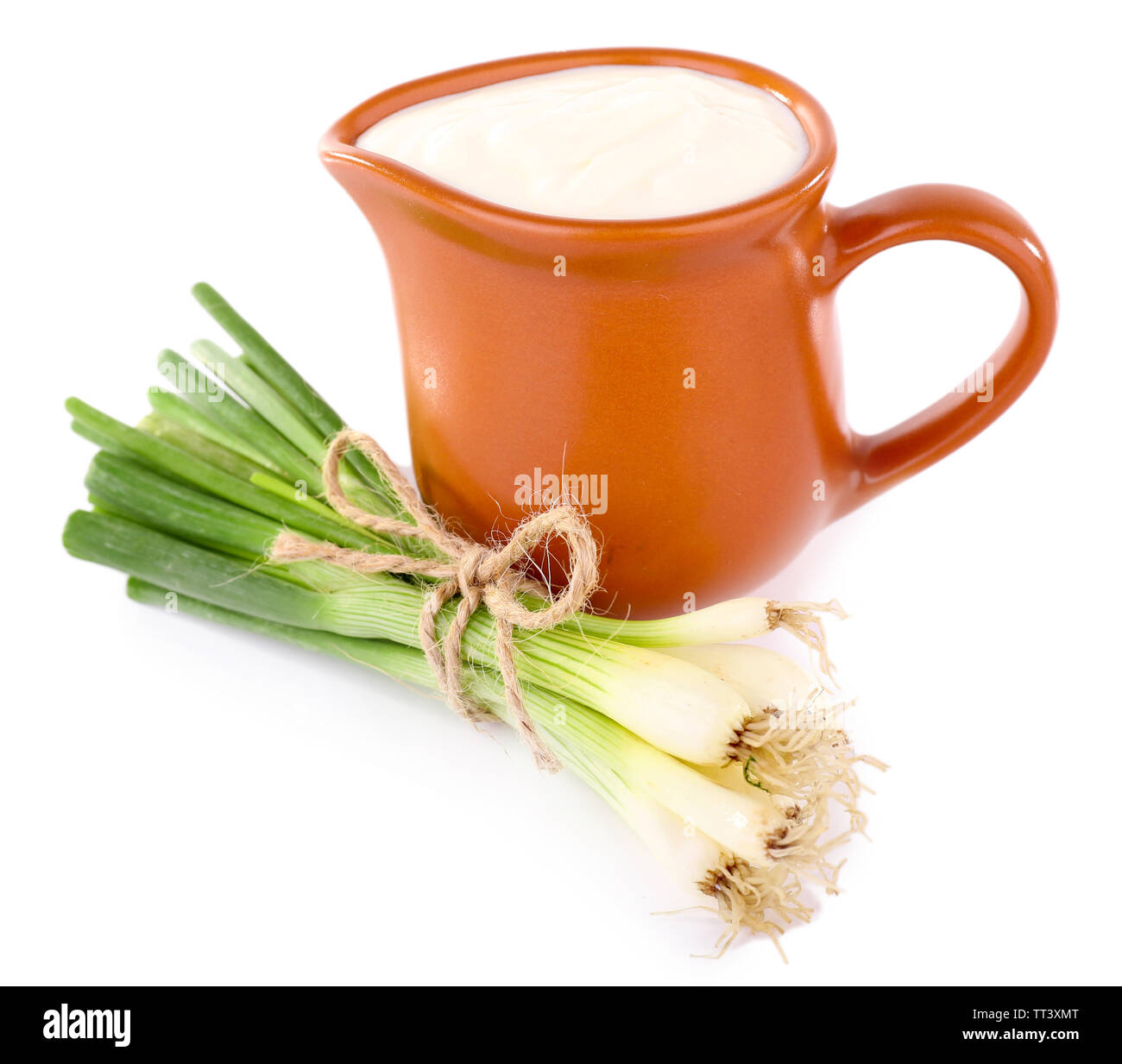 Clay pot with cream and a tuft of onion near it on white background ...