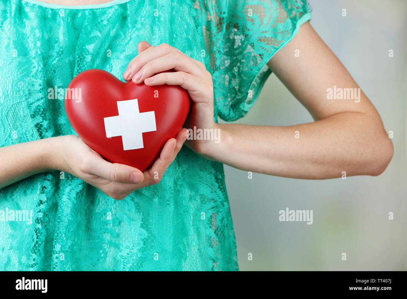 Red heart with cross sign in female hand, close-up, on light background ...