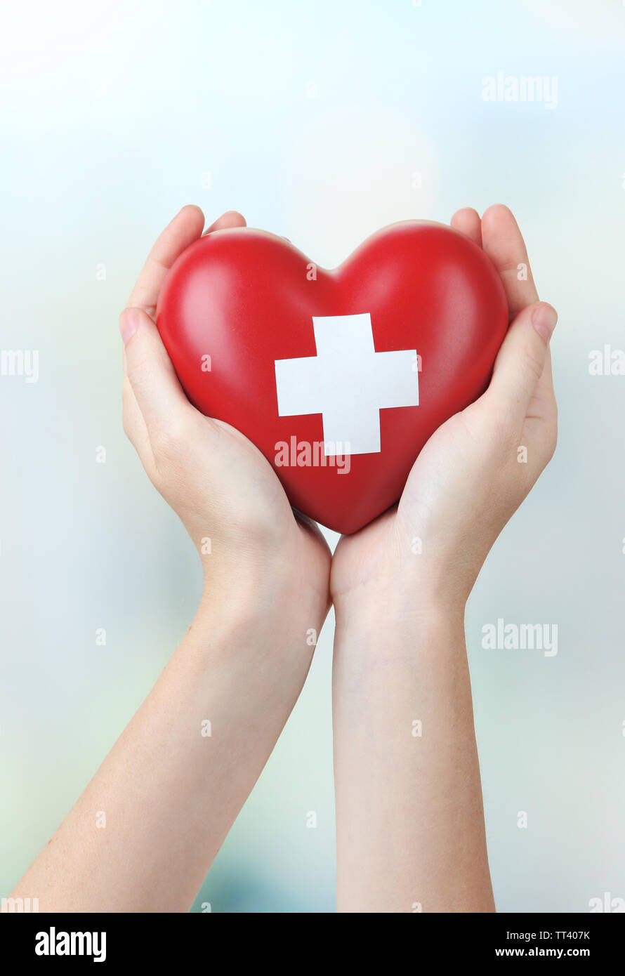 Red heart with cross sign in female hand, close-up, on light background ...