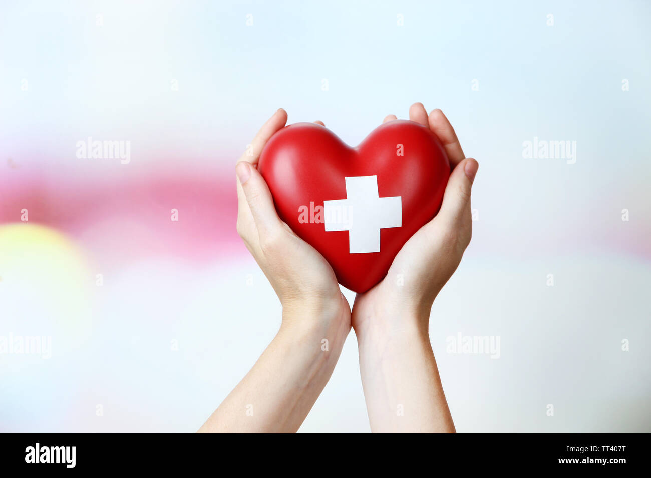 Red heart with cross sign in female hand, close-up, on light background ...