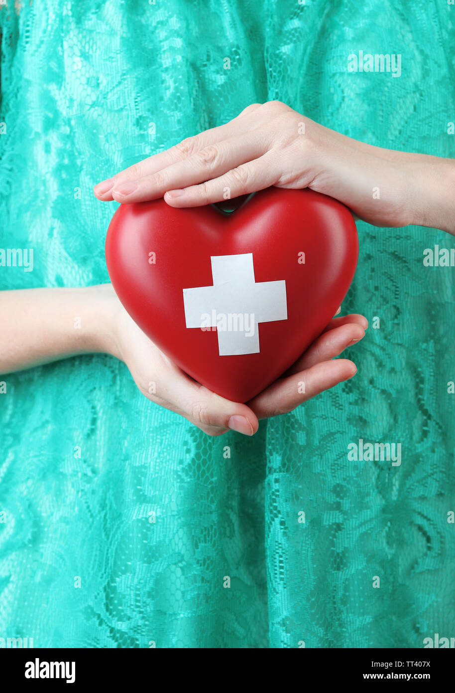 Red heart with cross sign in female hand, close-up, on light background ...