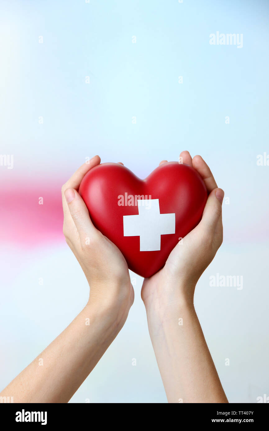 Red heart with cross sign in female hand, close-up, on light background ...