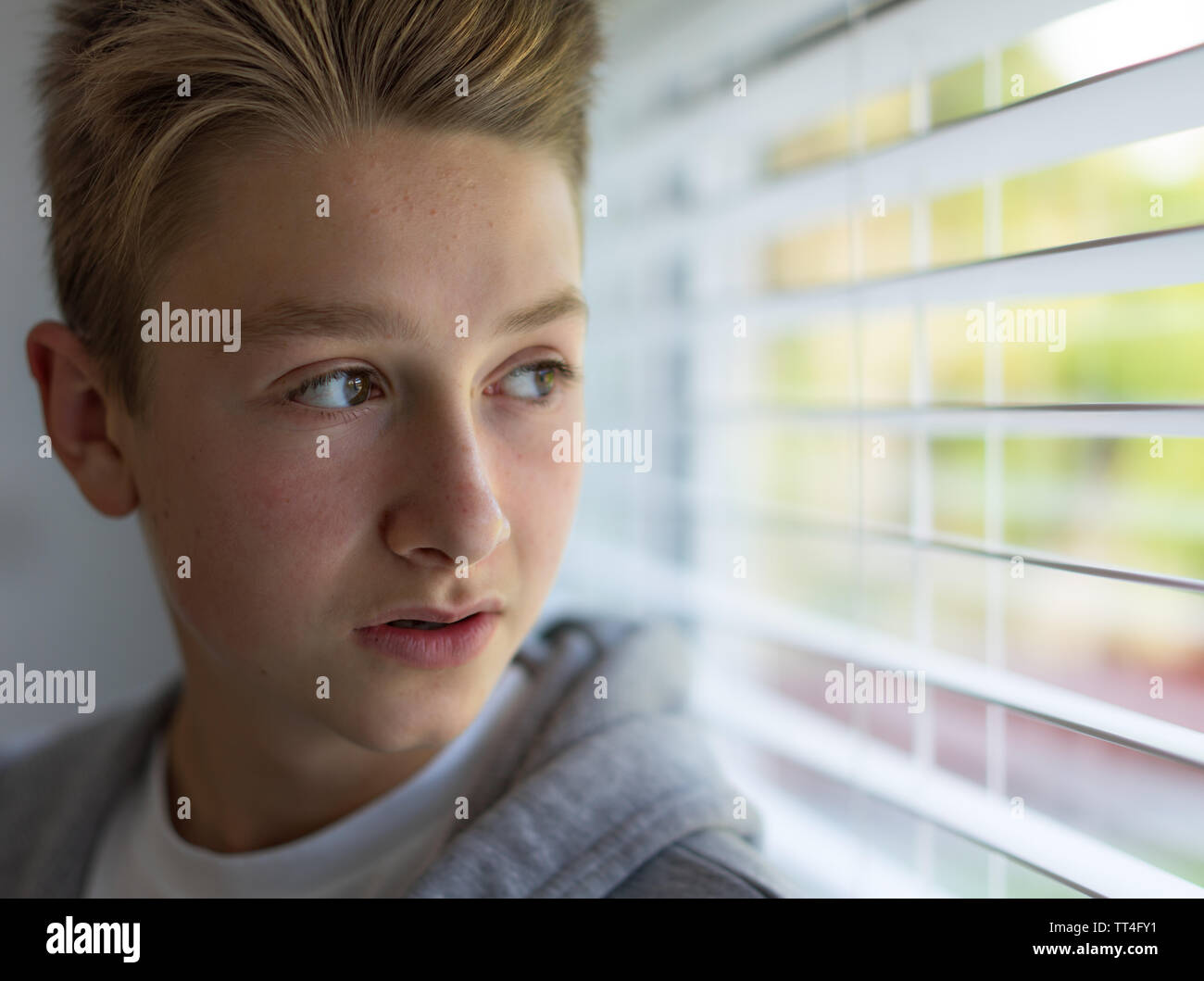 Boy looking out of a window through blinds Stock Photo - Alamy
