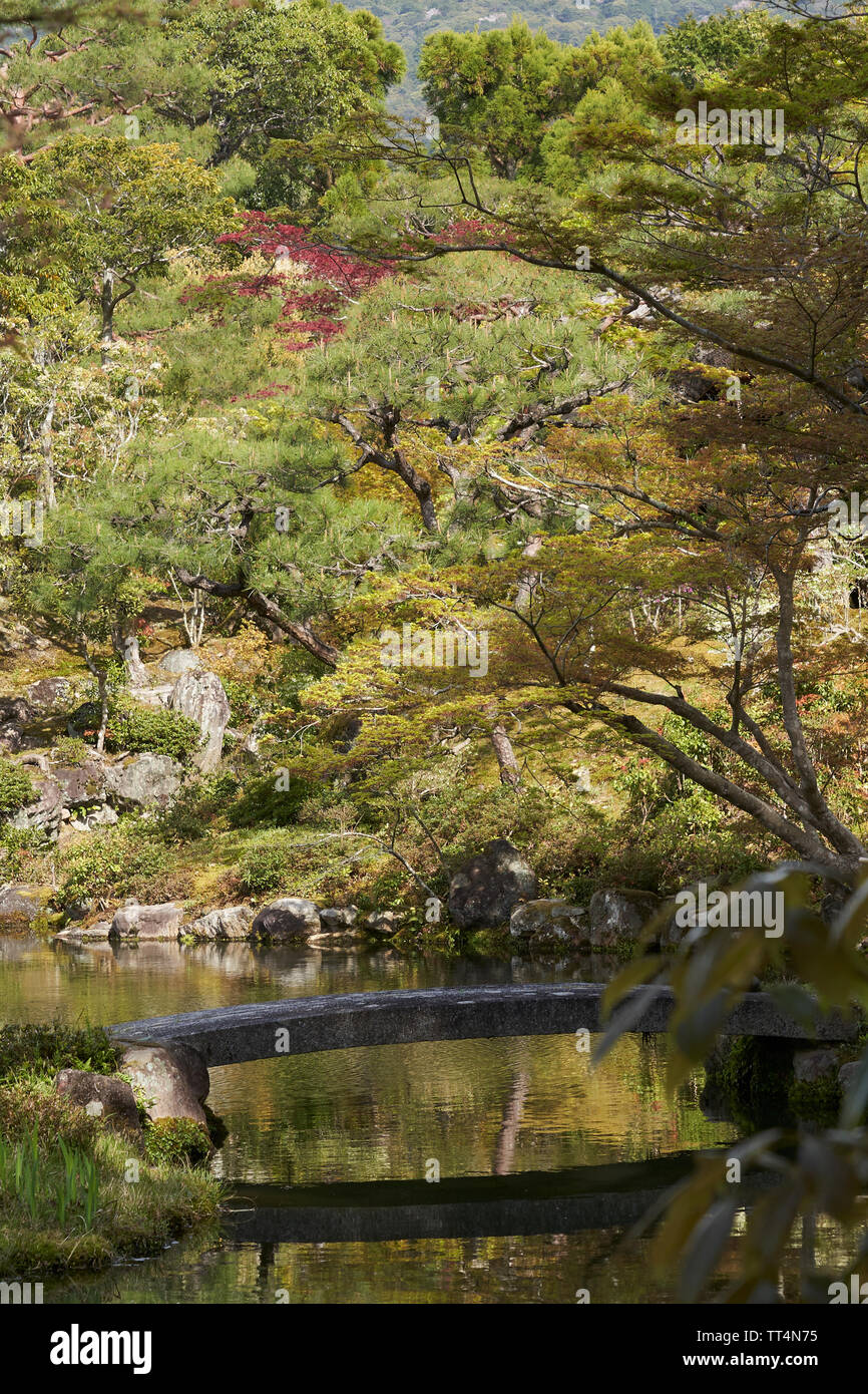 Japanese garden with a stone bridge across a river. Image is dominated ...
