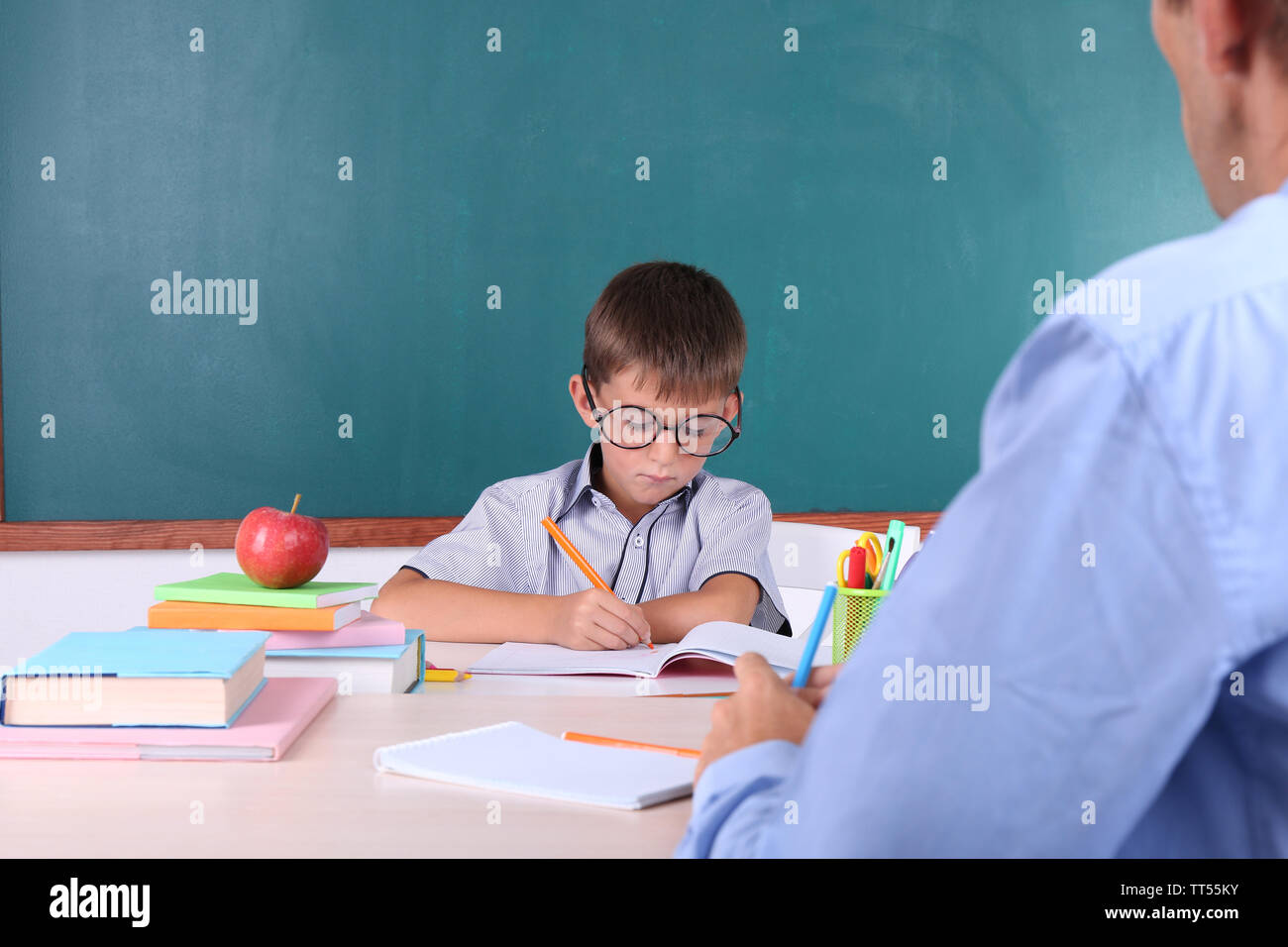 Schoolboy and teacher sitting in classroom on blackboard background ...