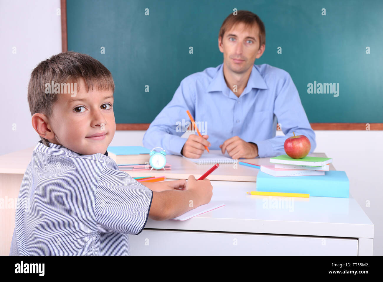 Schoolboy and teacher sitting in classroom on blackboard background ...