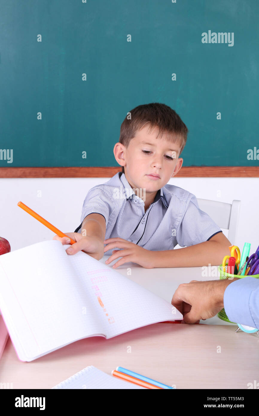 Schoolboy and teacher sitting in classroom on blackboard background ...
