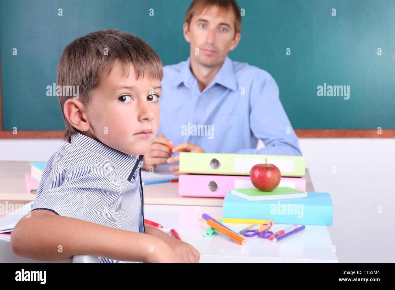 Schoolboy and teacher sitting in classroom on blackboard background ...