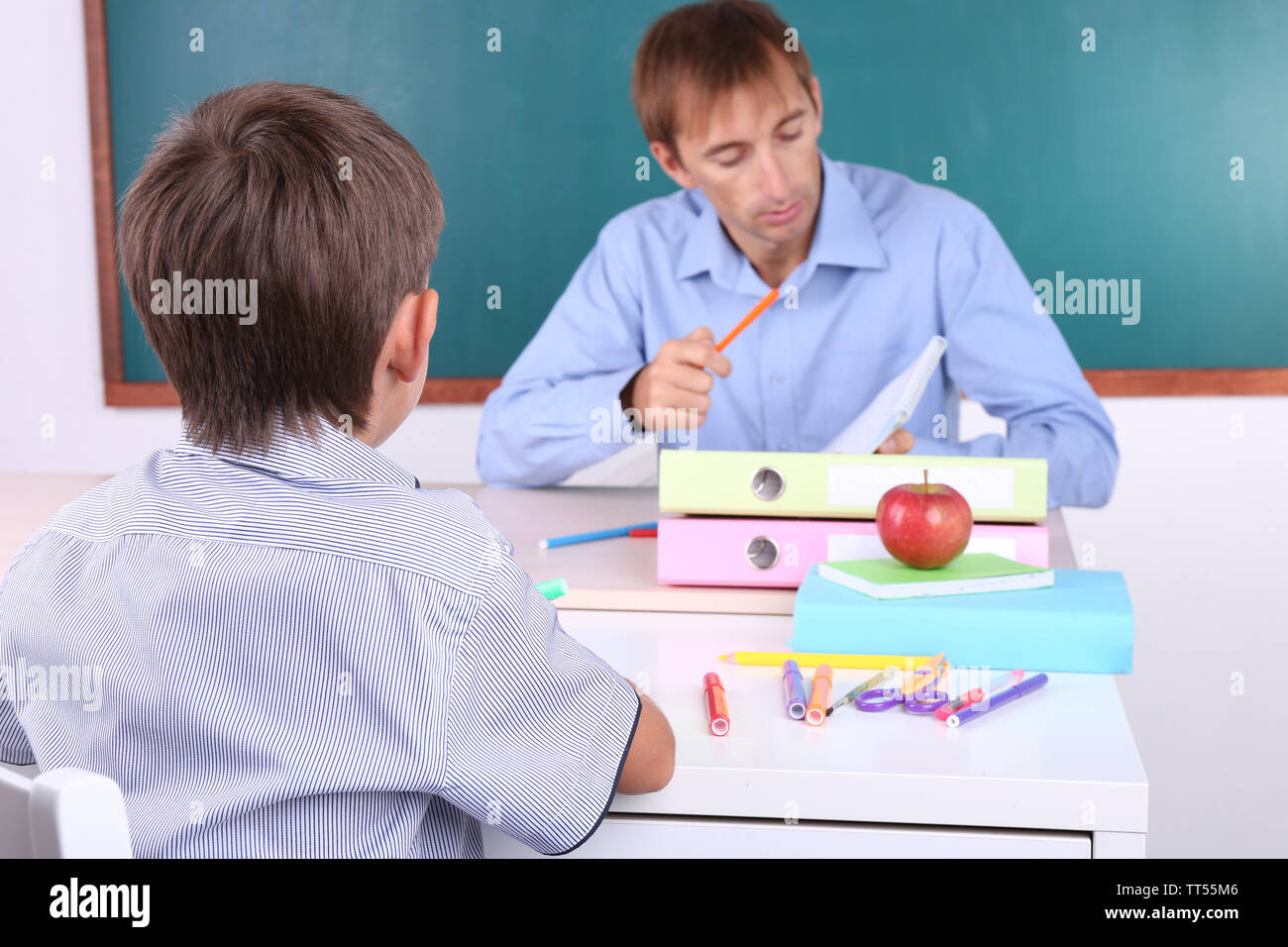 Schoolboy and teacher sitting in classroom on blackboard background ...