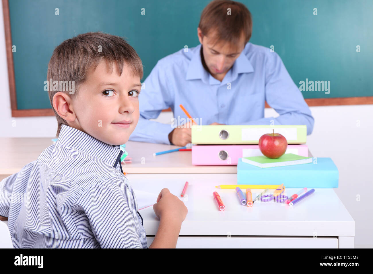 Schoolboy and teacher sitting in classroom on blackboard background ...