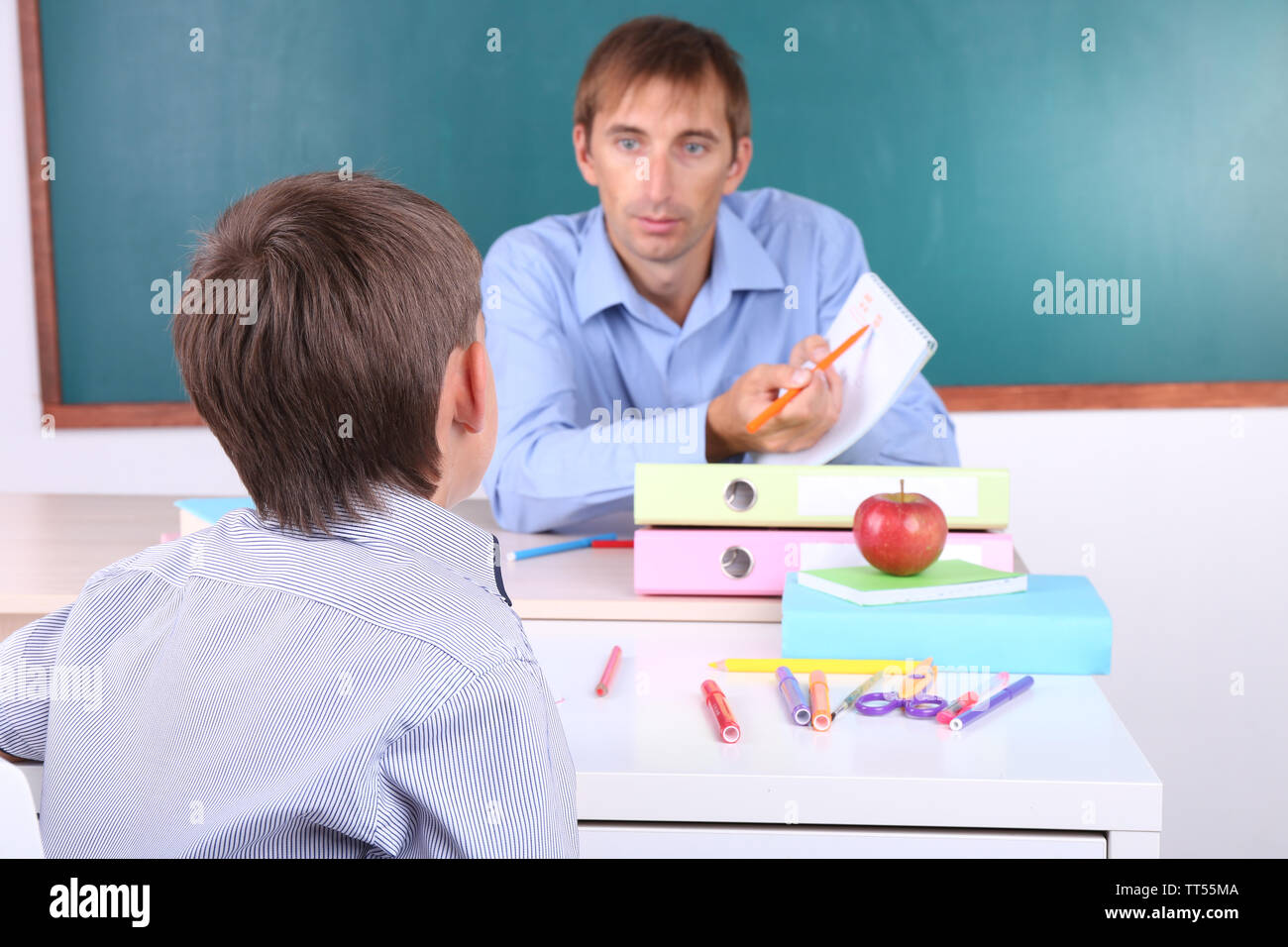 Schoolboy and teacher sitting in classroom on blackboard background ...