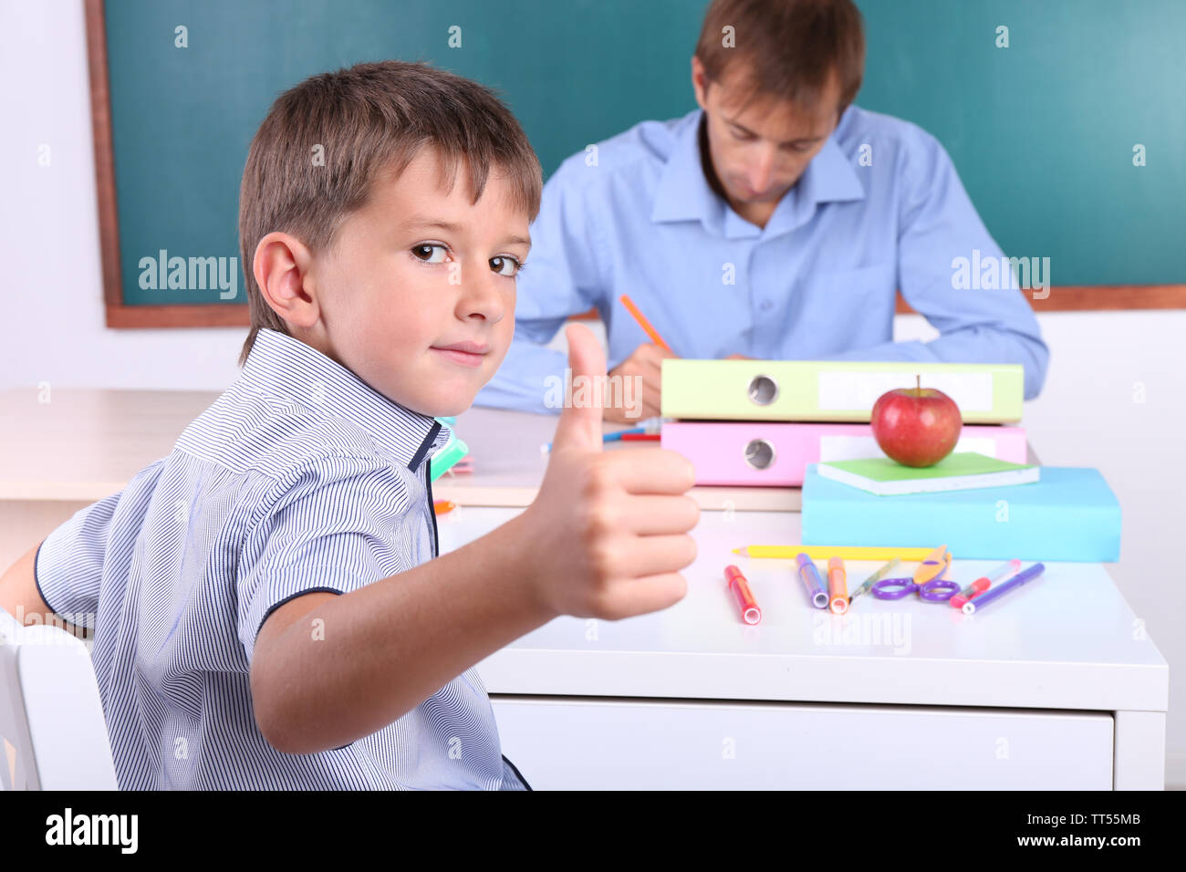 Schoolboy and teacher sitting in classroom on blackboard background ...
