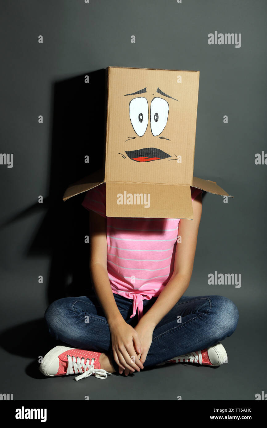 Woman with cardboard box on her head with sad face, on grey background ...