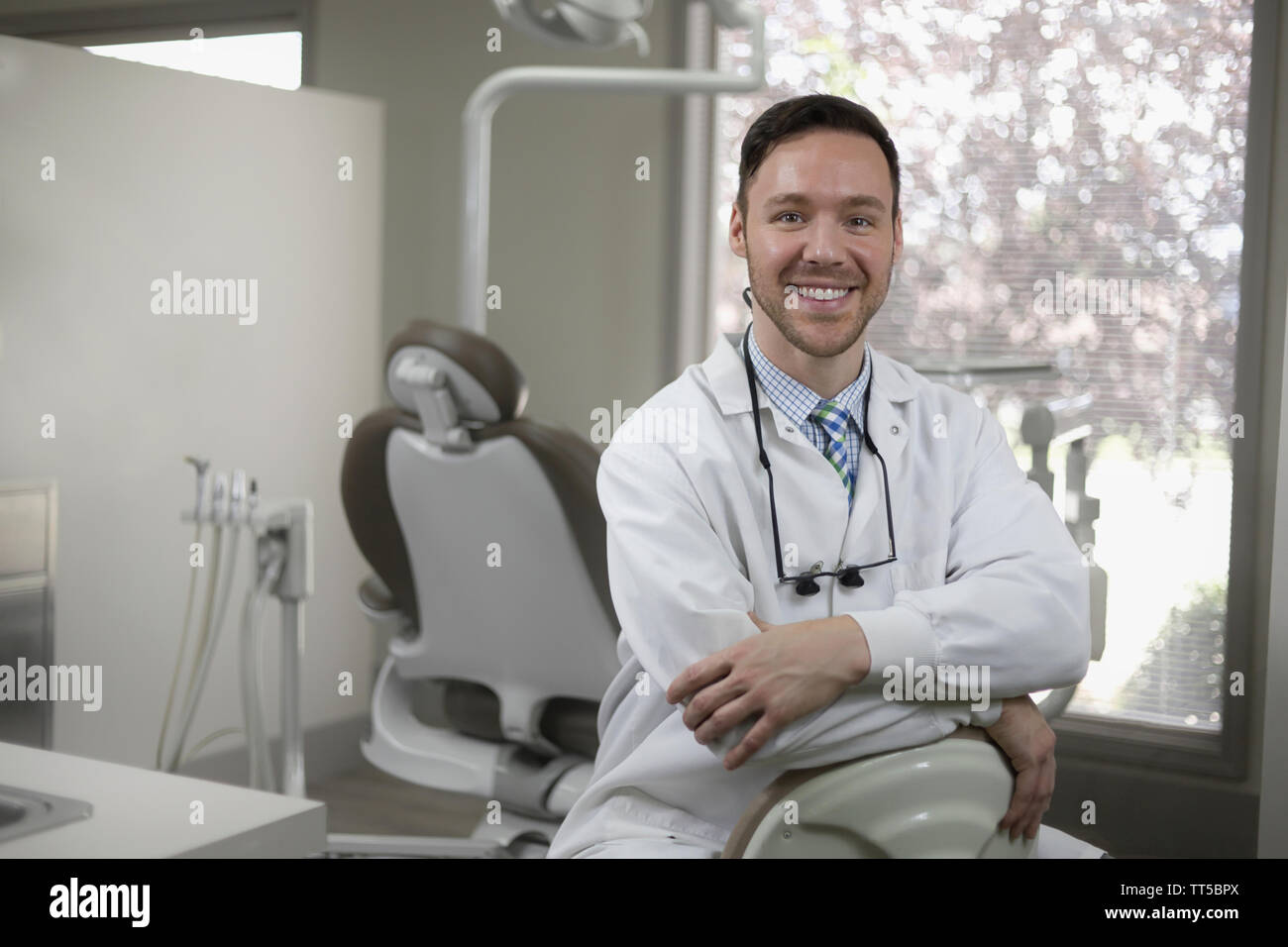 Portrait of friendly dentist in a modern clinic, sitting Stock Photo ...