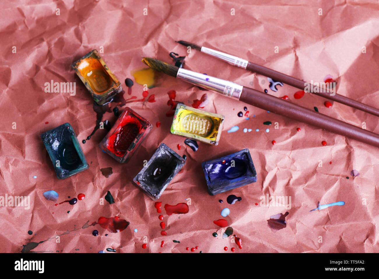 Watercolor paint cubes with brushes and spilled paint on brown paper ...