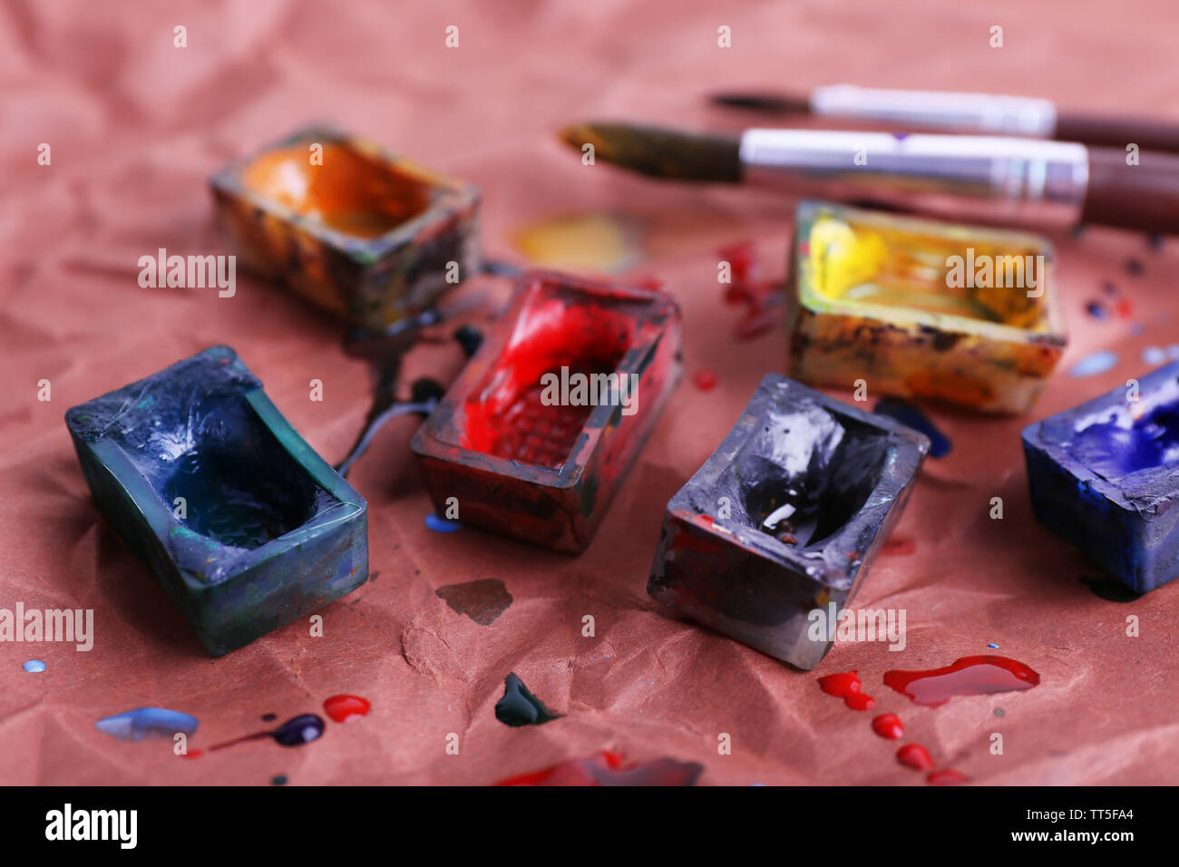 Watercolor paint cubes with brushes and spilled paint on brown paper ...