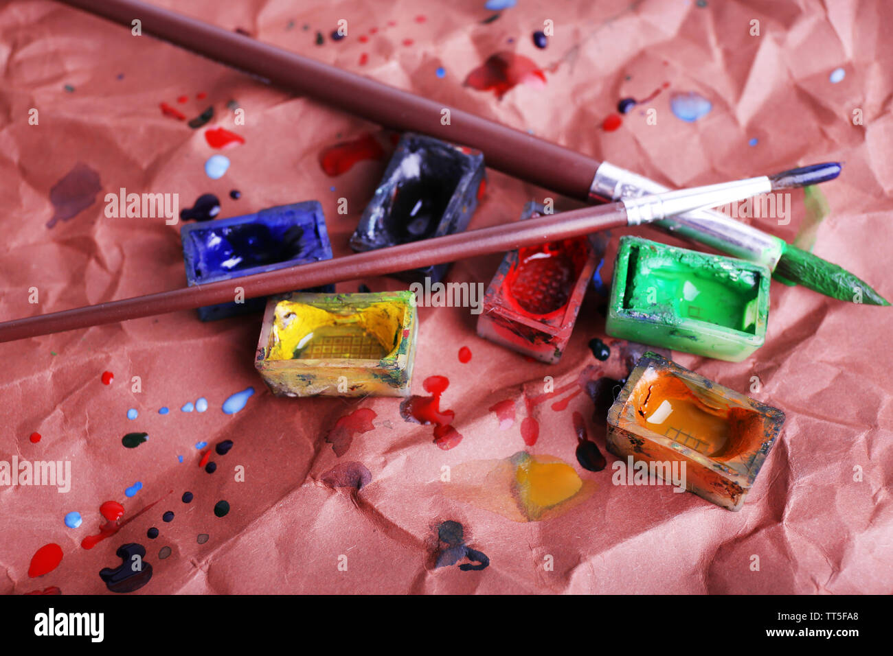 Watercolor paint cubes with brushes and spilled paint on brown paper ...