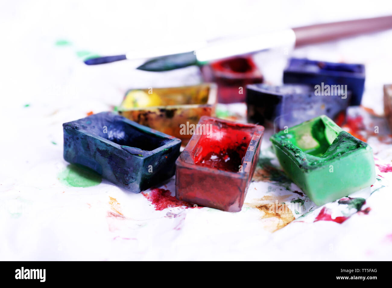 Watercolor paint cubes with brushes and spilled paint on white paper ...
