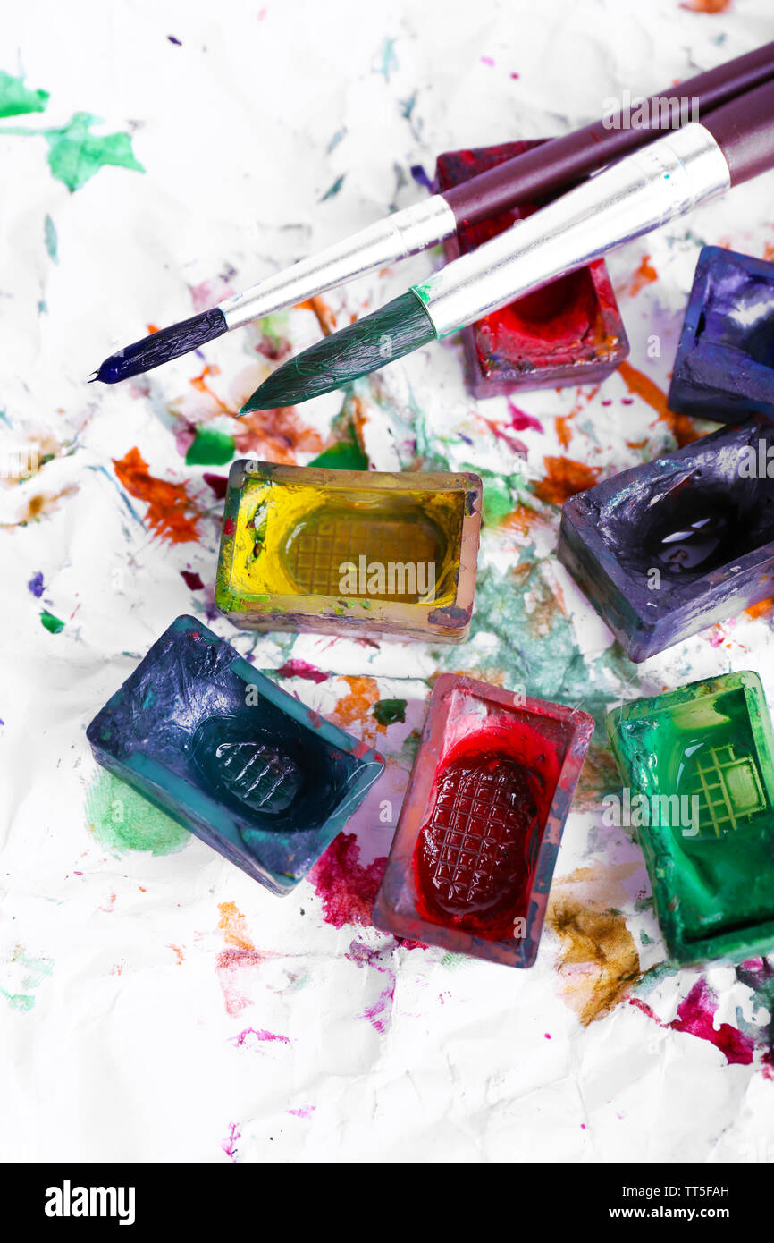 Watercolor paint cubes with brushes and spilled paint on white paper ...
