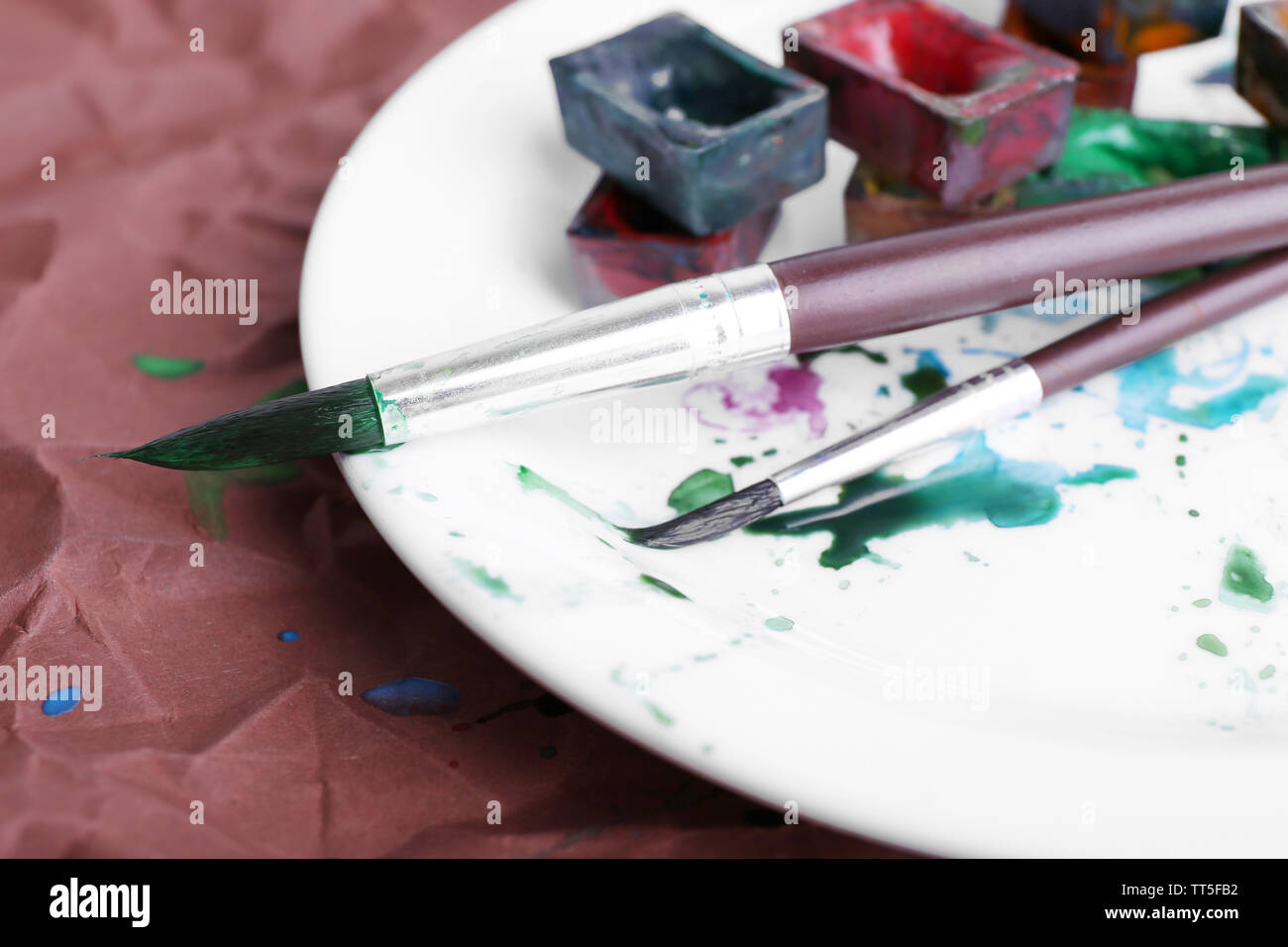 Watercolor paint cubes with brushes on plate on brown paper background ...