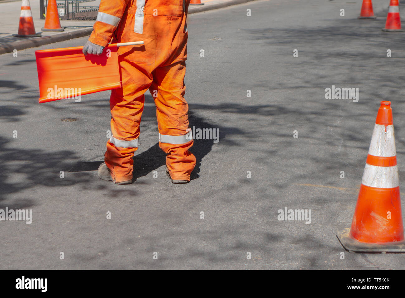 road worker directing traffic with orange flag and reflective suit ...