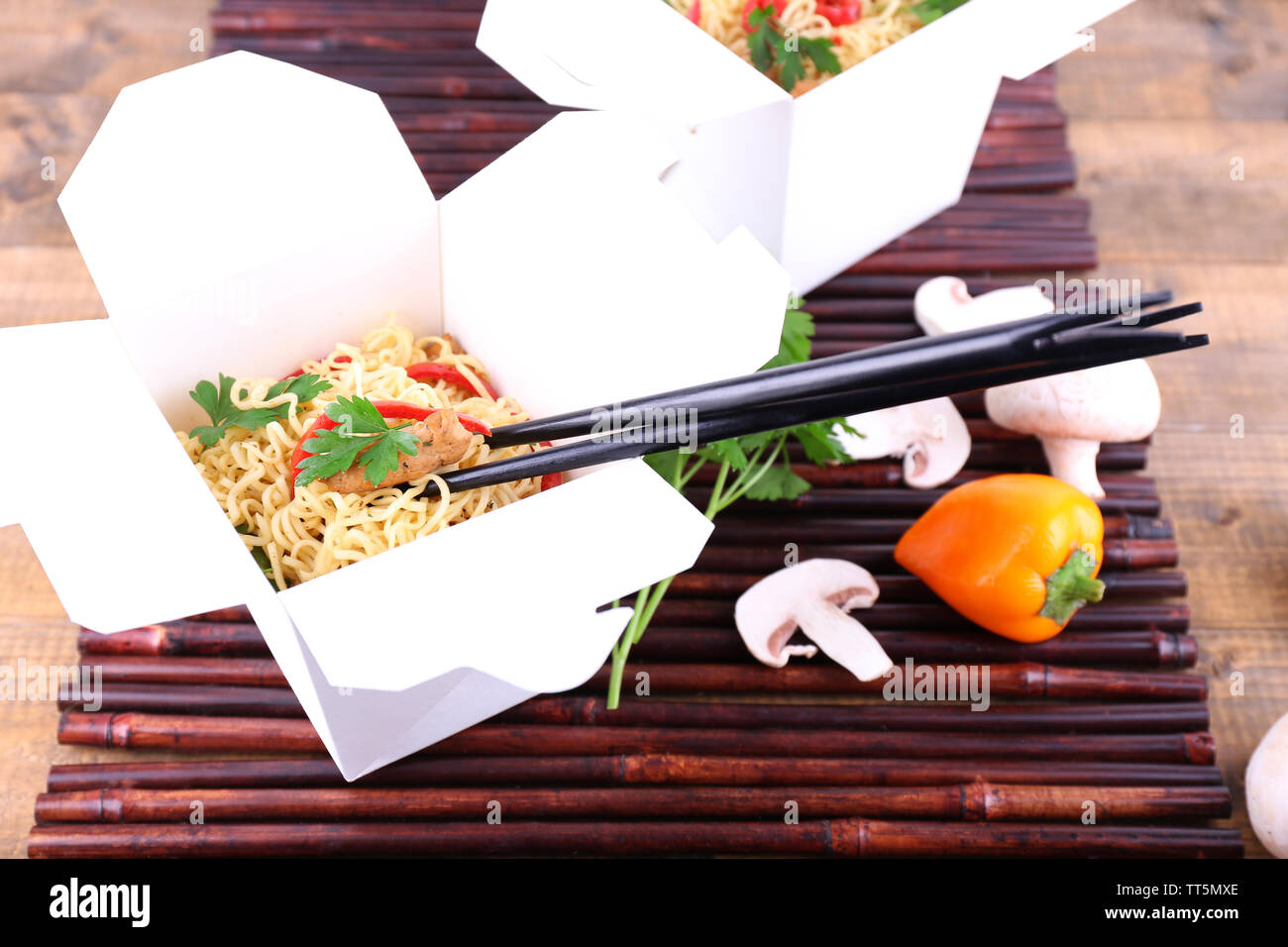 Chinese noodles in takeaway boxes on bamboo mat on wooden background ...