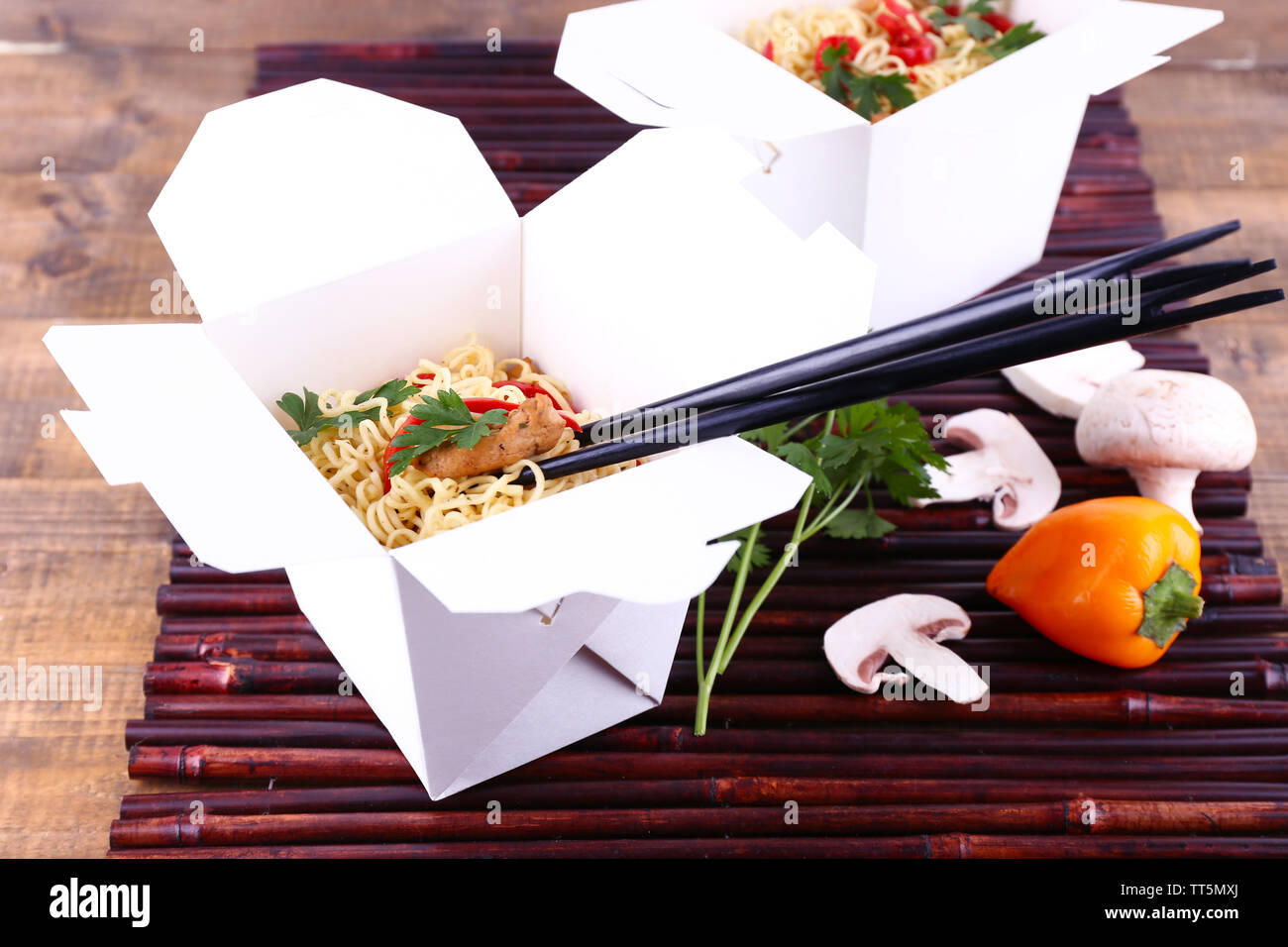 Chinese noodles in takeaway boxes on bamboo mat on wooden background ...