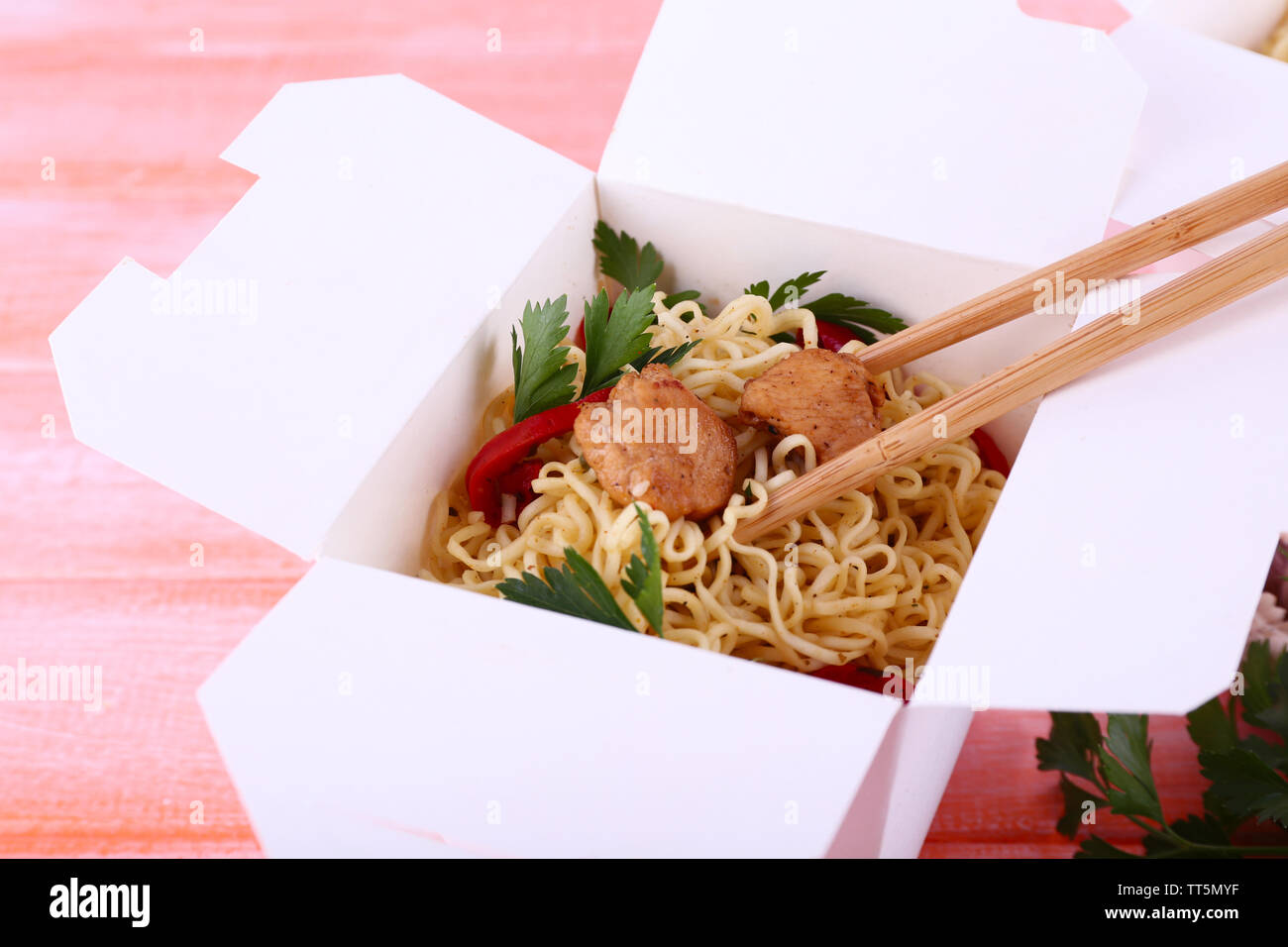 Chinese noodles with meat and pepper in takeaway box on pink background ...