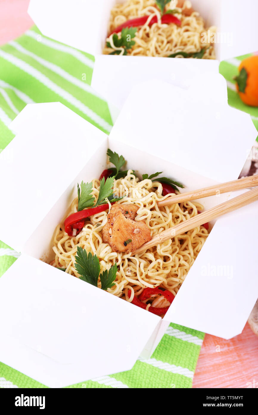 Chinese noodles and sticks in takeaway boxes on green napkin on pink ...