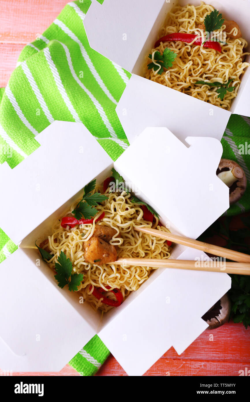Chinese noodles and sticks in takeaway boxes on green napkin on pink ...