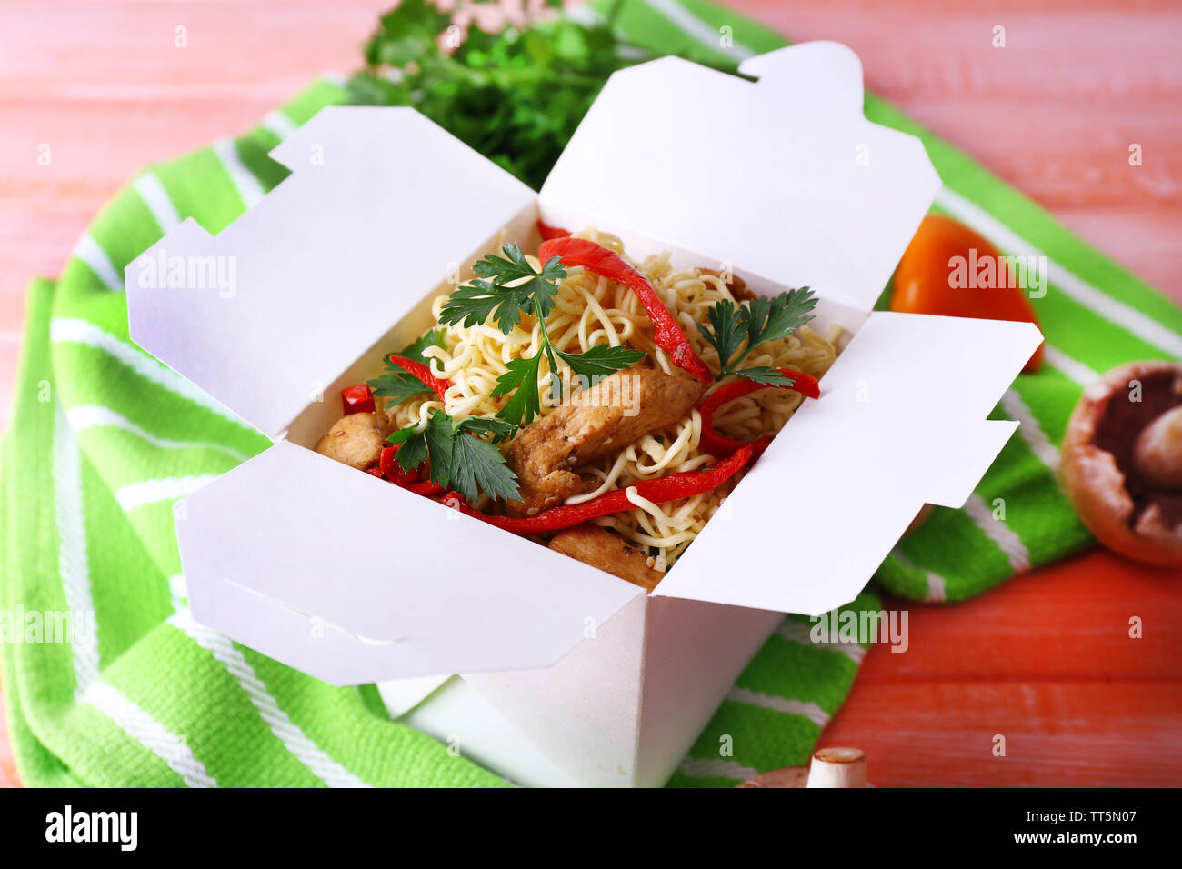 Chinese noodles in takeaway box on green napkin on pink background ...