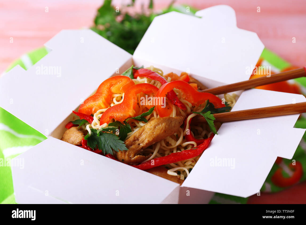 Chinese noodles and sticks in takeaway box on green napkin on pink ...